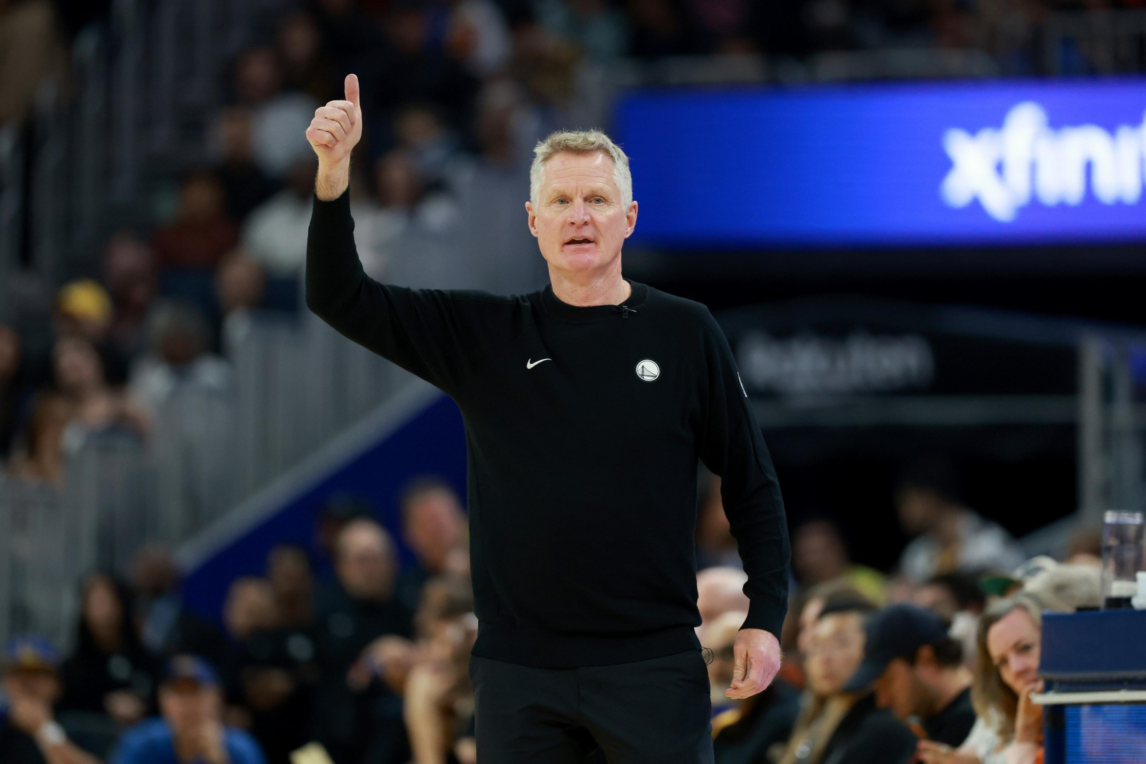 A man in a black long-sleeve shirt with a small logo raises his right ...