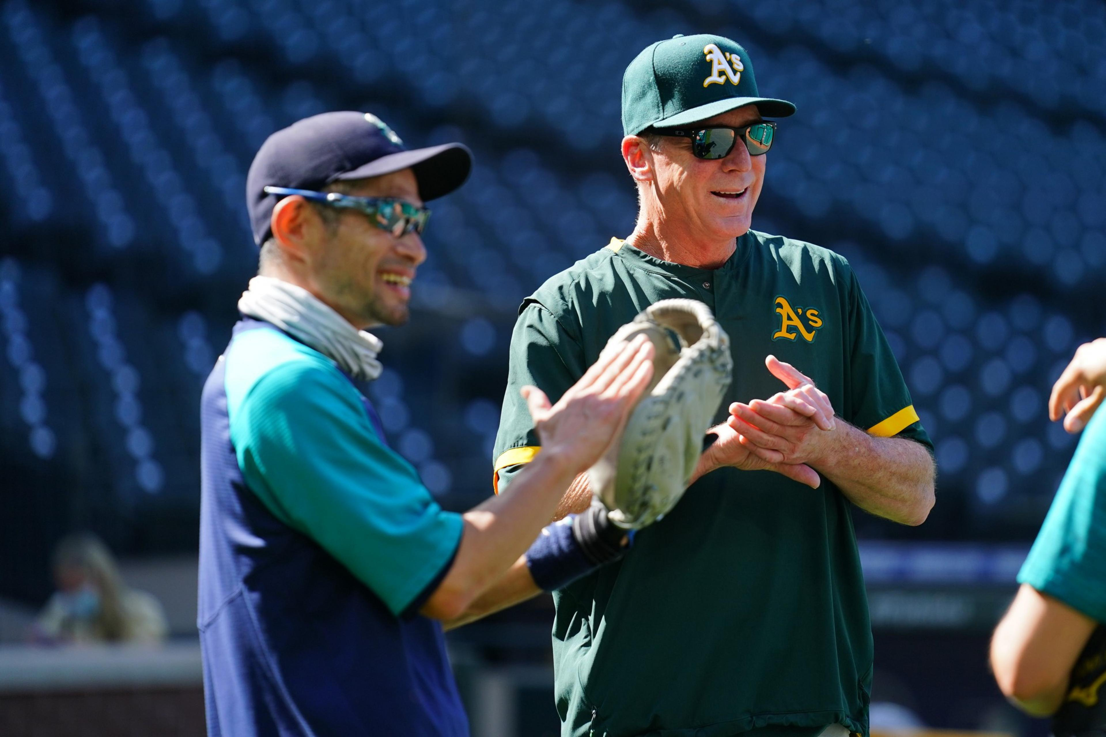 Two men in baseball attire smile and clap, one wearing an Oakland ...