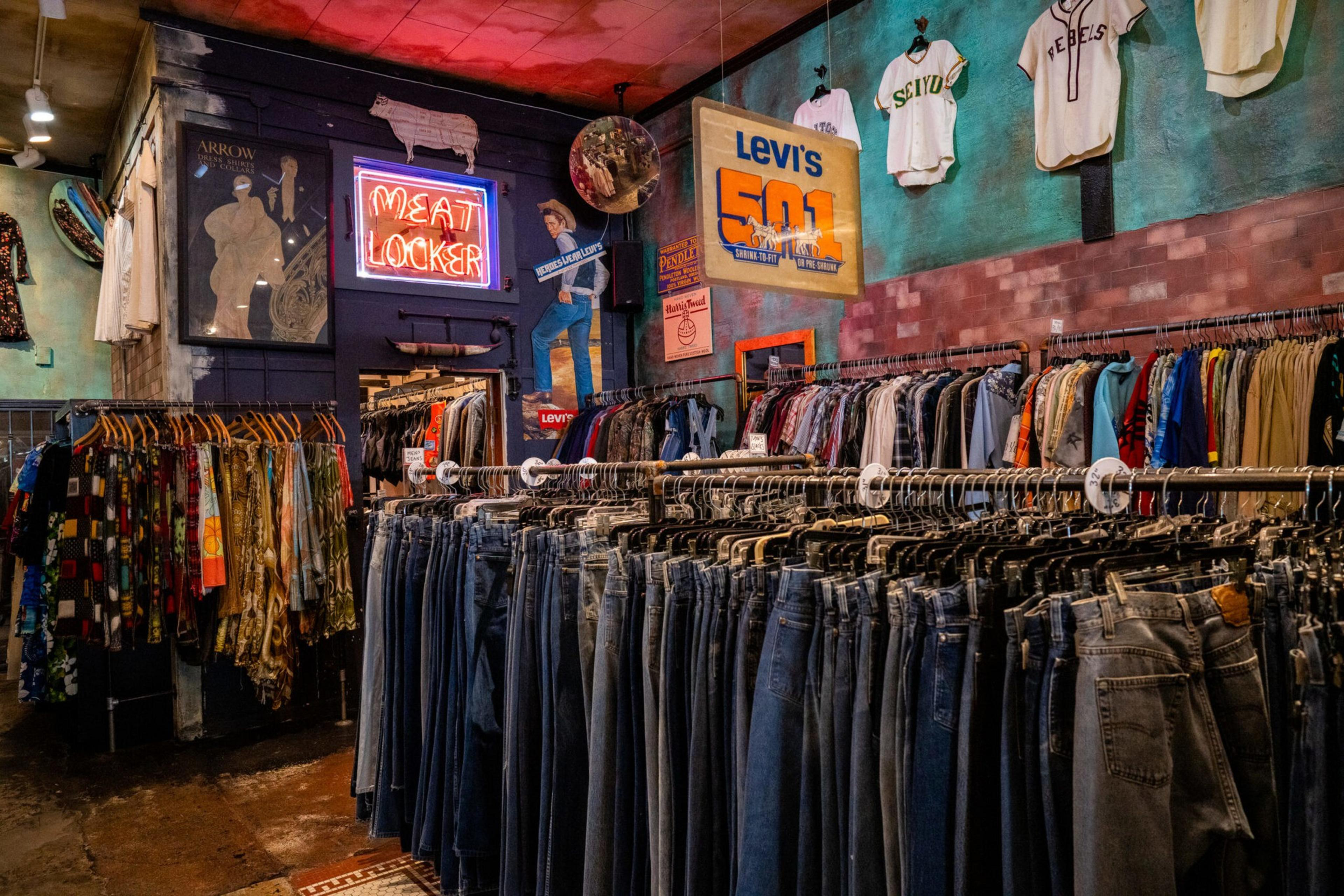 Rows of denim jeans and various clothes hang neatly in a vintage store ...