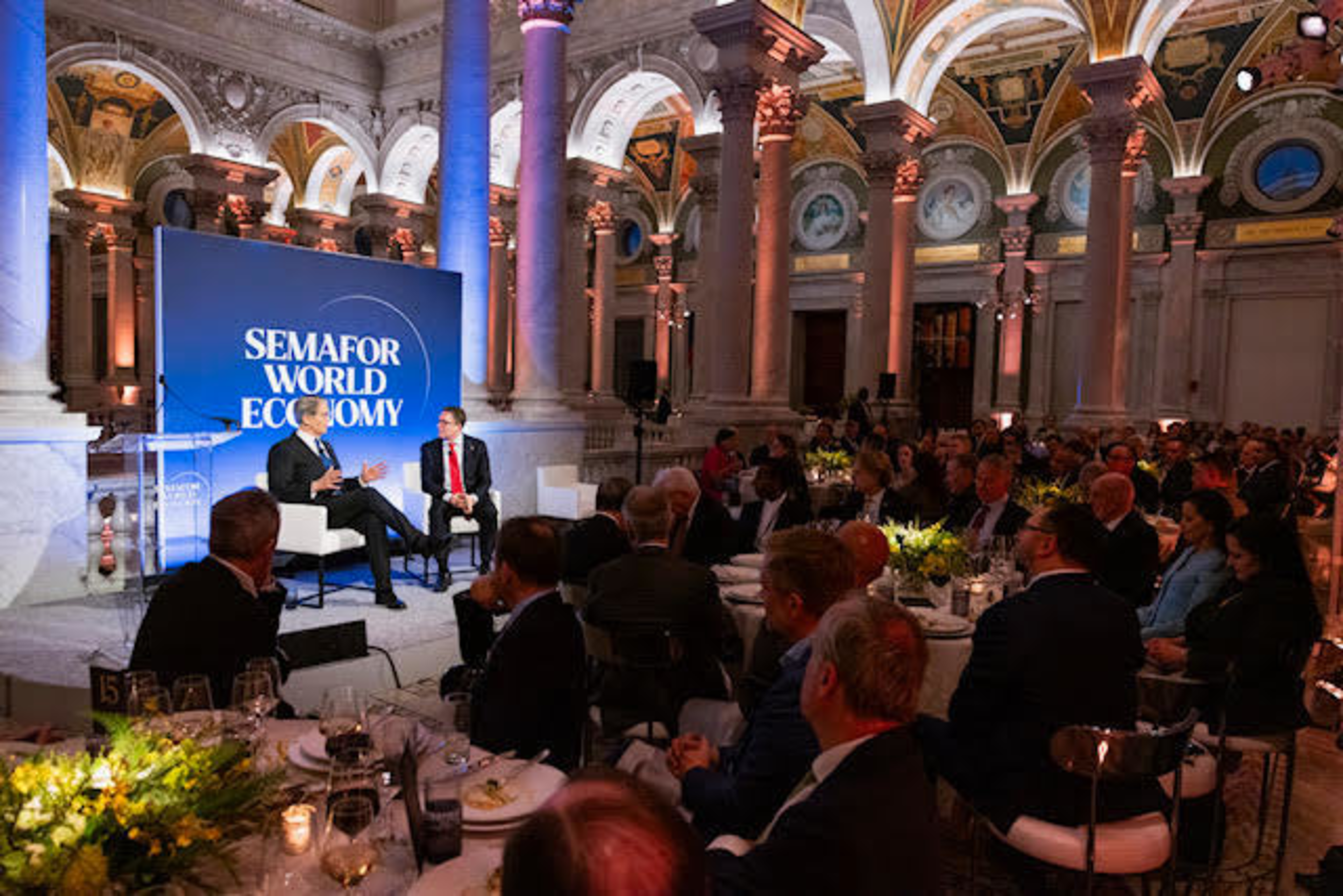 Two men in suits are seated on stage speaking at a Semafor World ...
