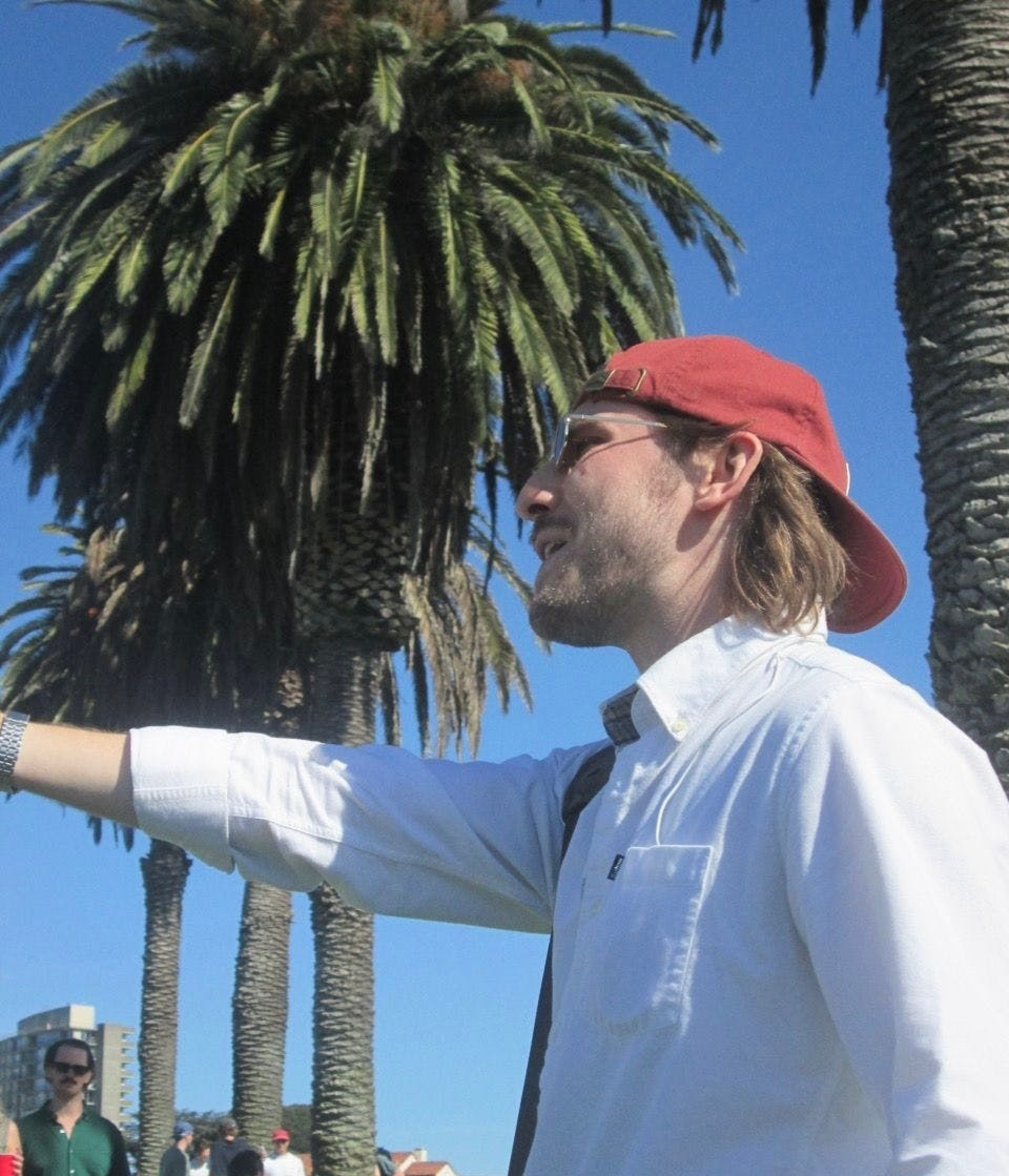 A man wearing a red backward cap, sunglasses, and white shirt reaches ...