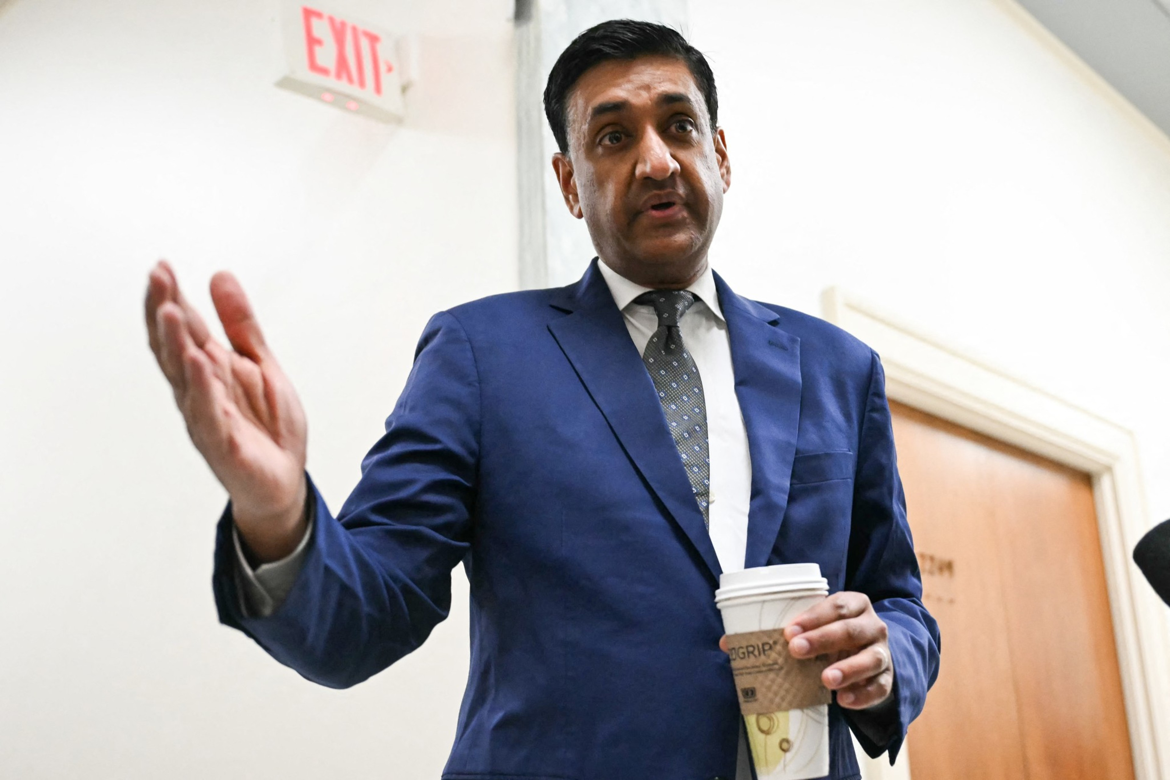 A man in a blue suit and patterned tie holds a coffee cup in one hand ...