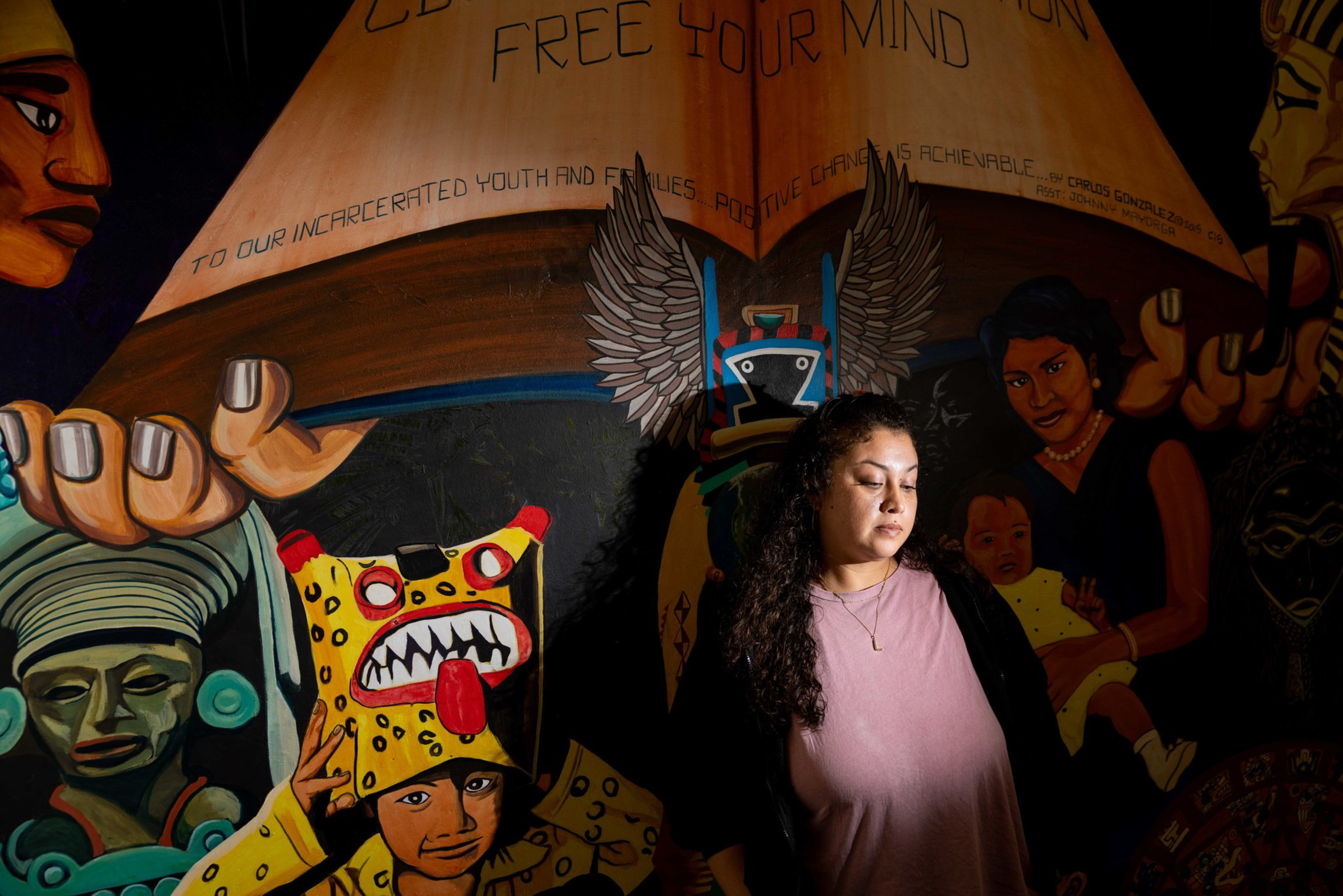 A woman with long curly hair stands with her eyes closed against a ...