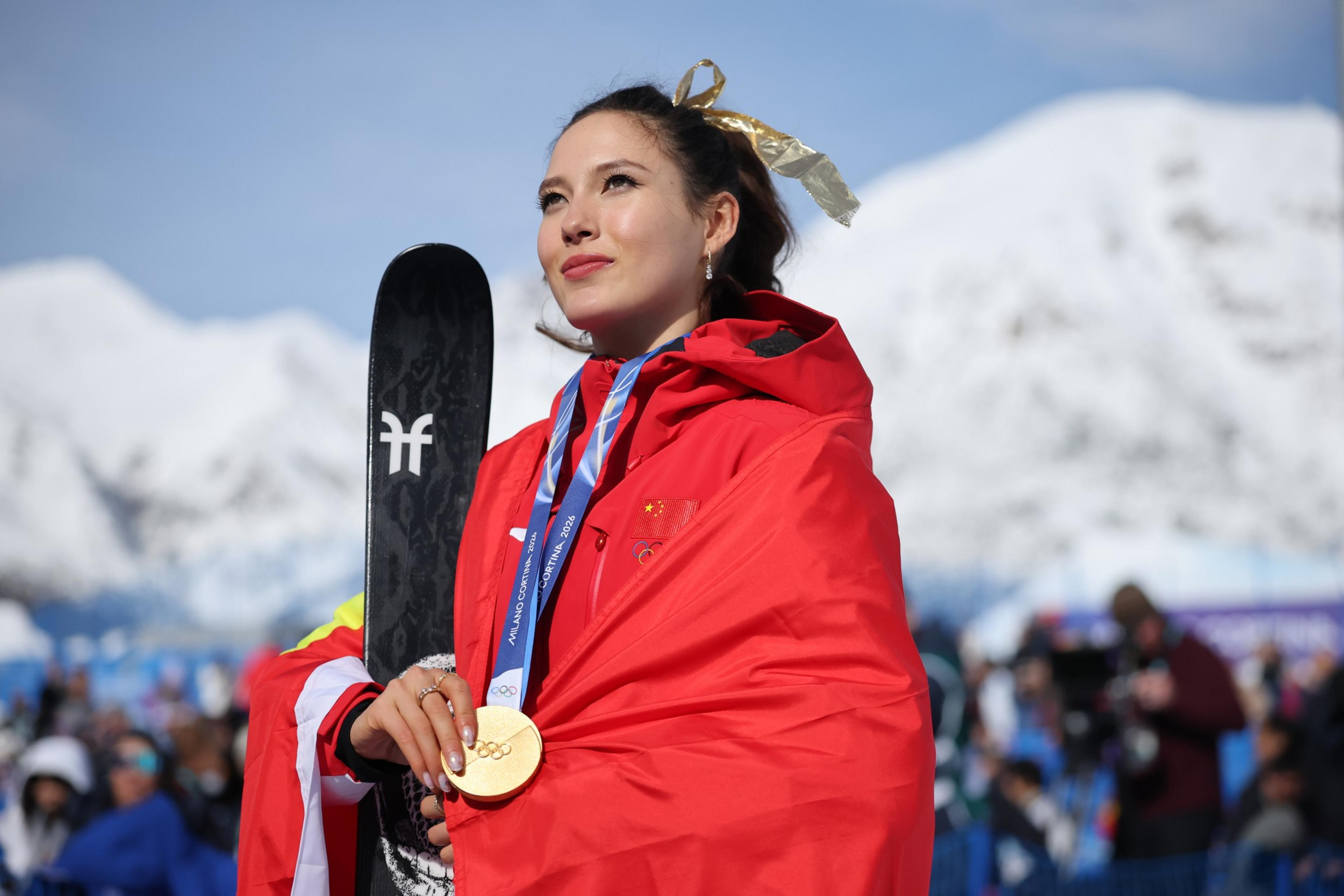 A woman wrapped in a red flag holds a ski and wears a gold Olympic ...