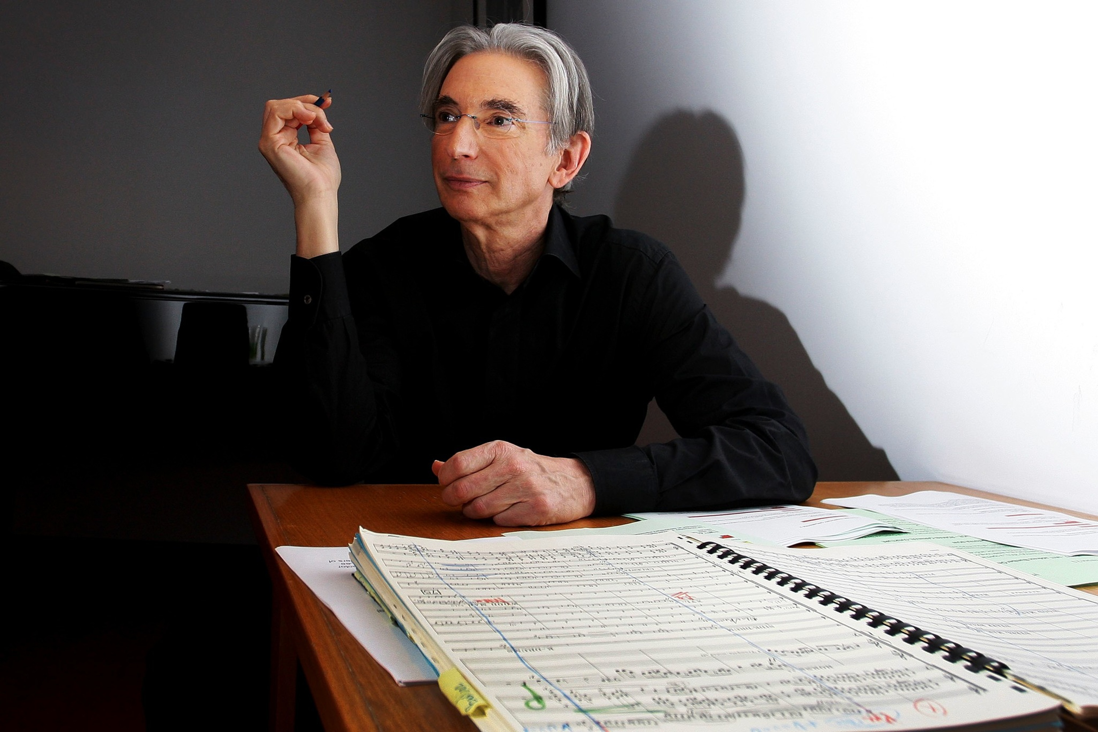 A man with gray hair and glasses sits at a table with music sheets ...