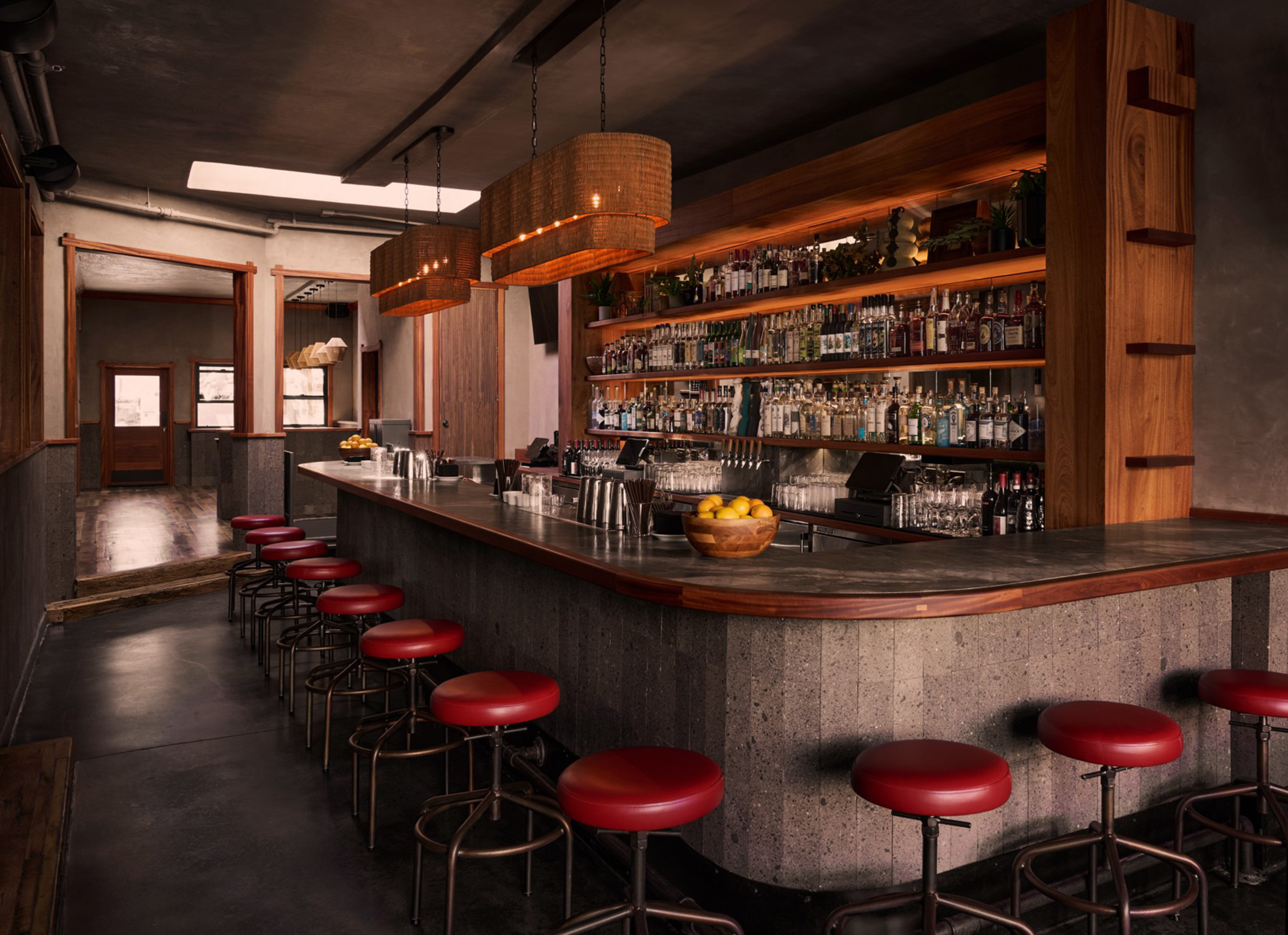 A sleek bar with concrete counters, red cushioned stools, wooden ...