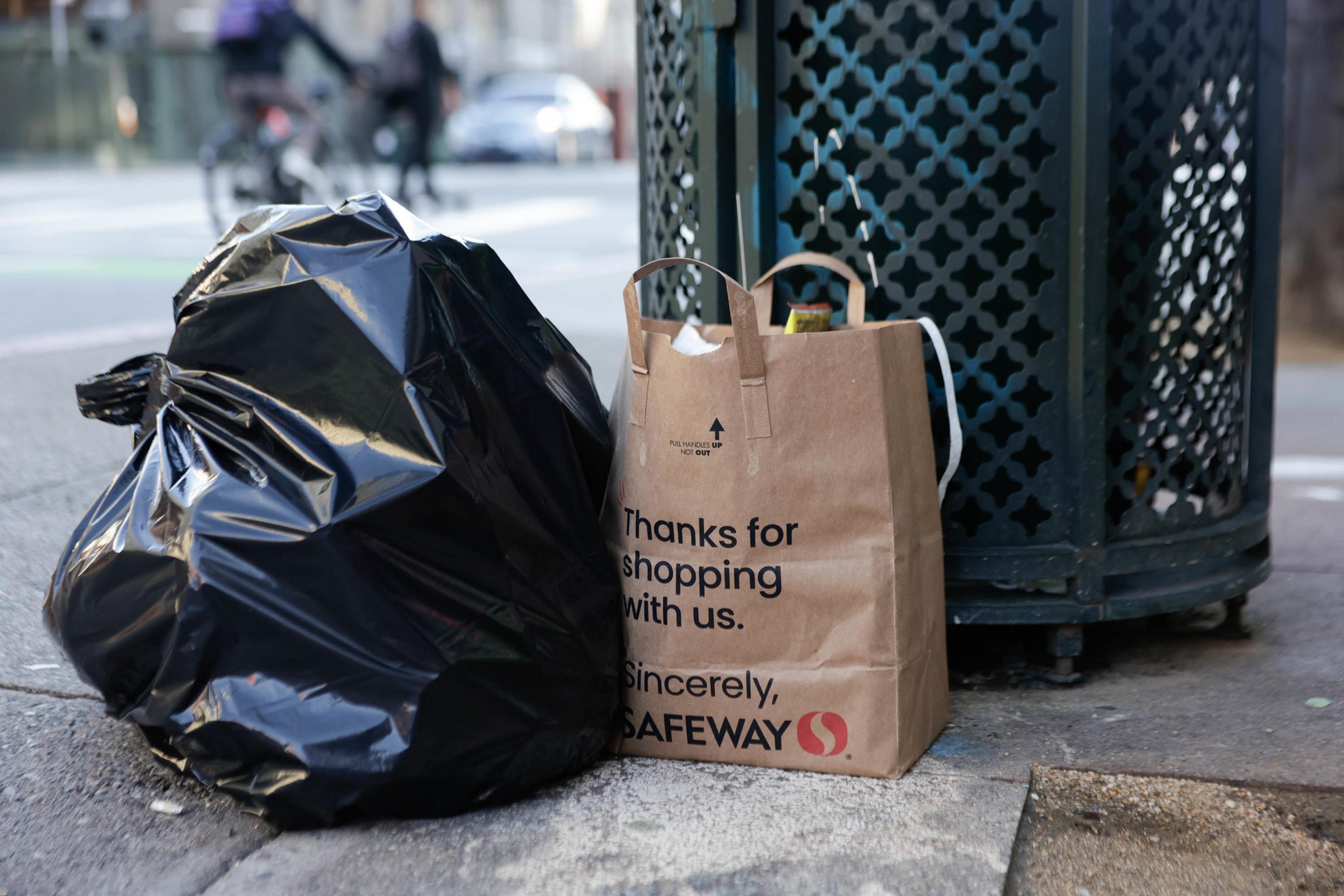 A black garbage bag and a brown paper Safeway bag full of items sit on ...