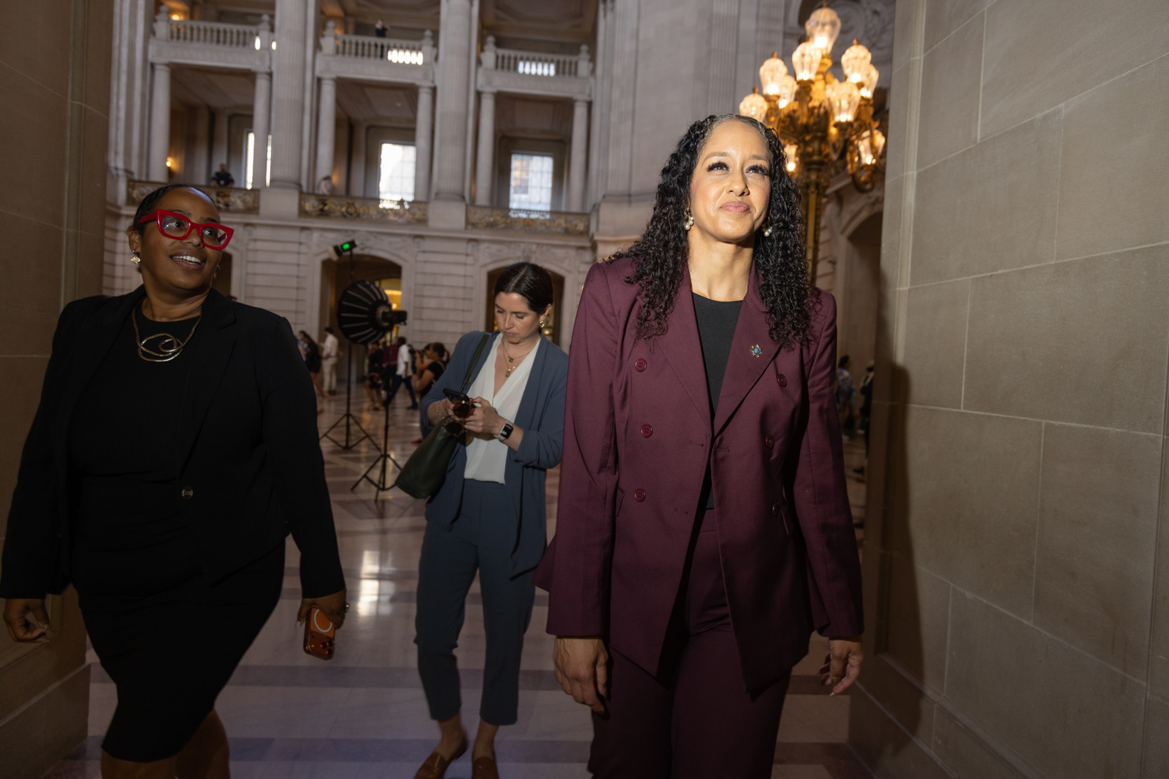 Three women walk through a grand hallway with marble floors and ...