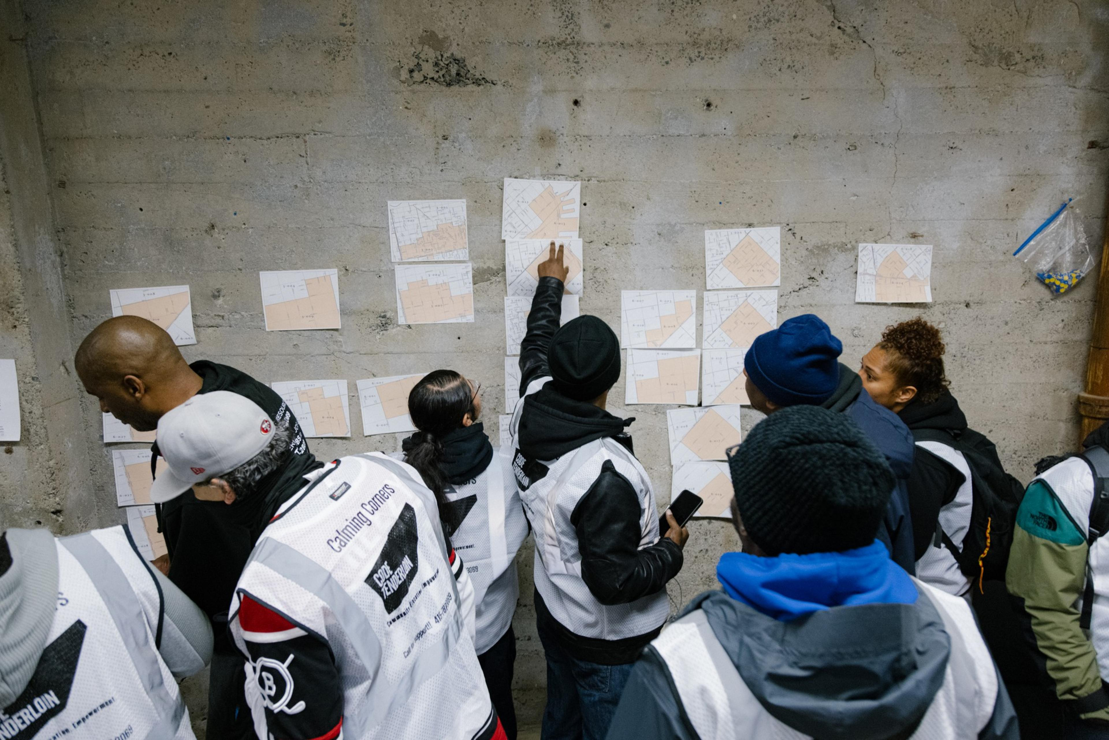 Several people wearing white vests examine and discuss hand-drawn maps ...