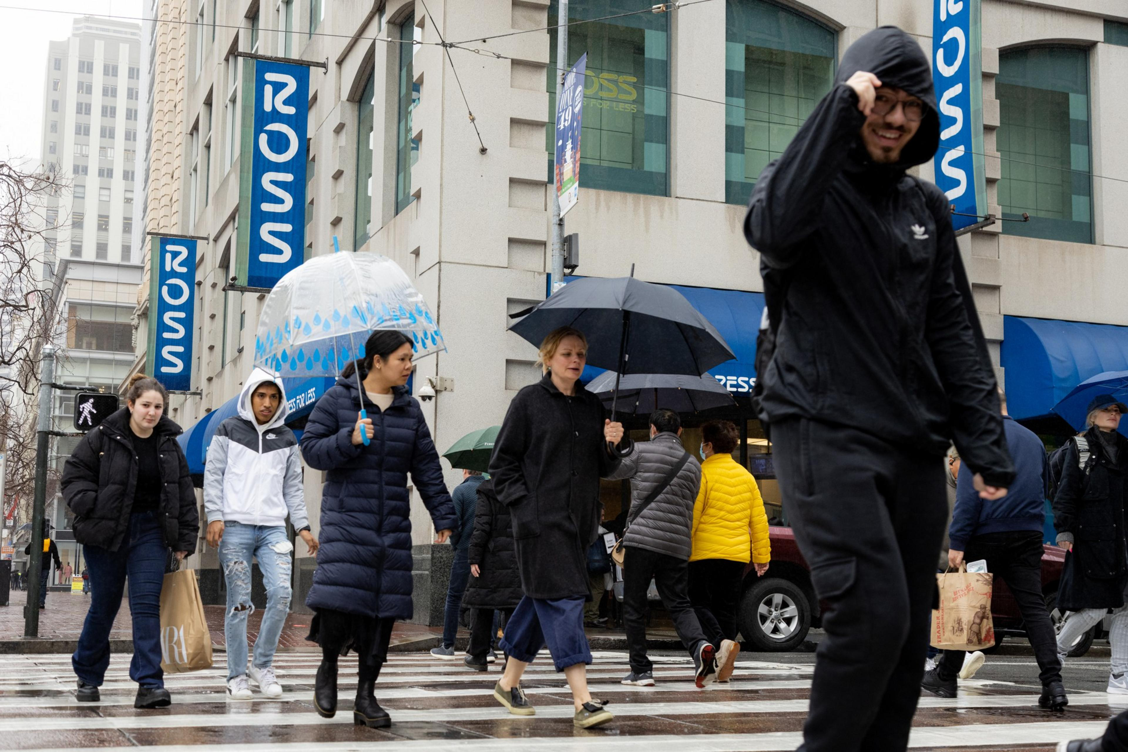 People wearing coats and carrying umbrellas walk across a city street ...