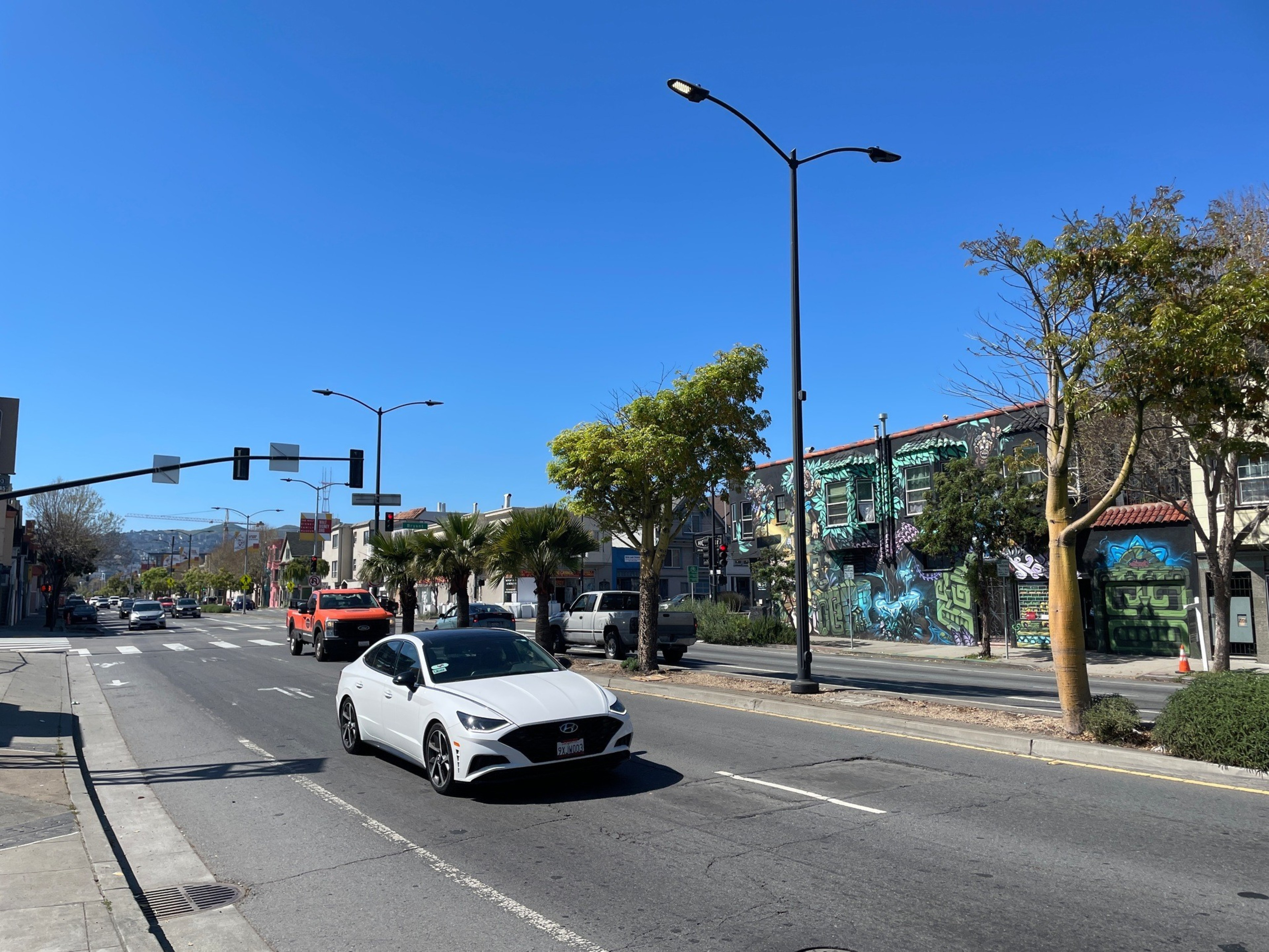 A white car drives on a sunny street lined with palm trees, colorful ...