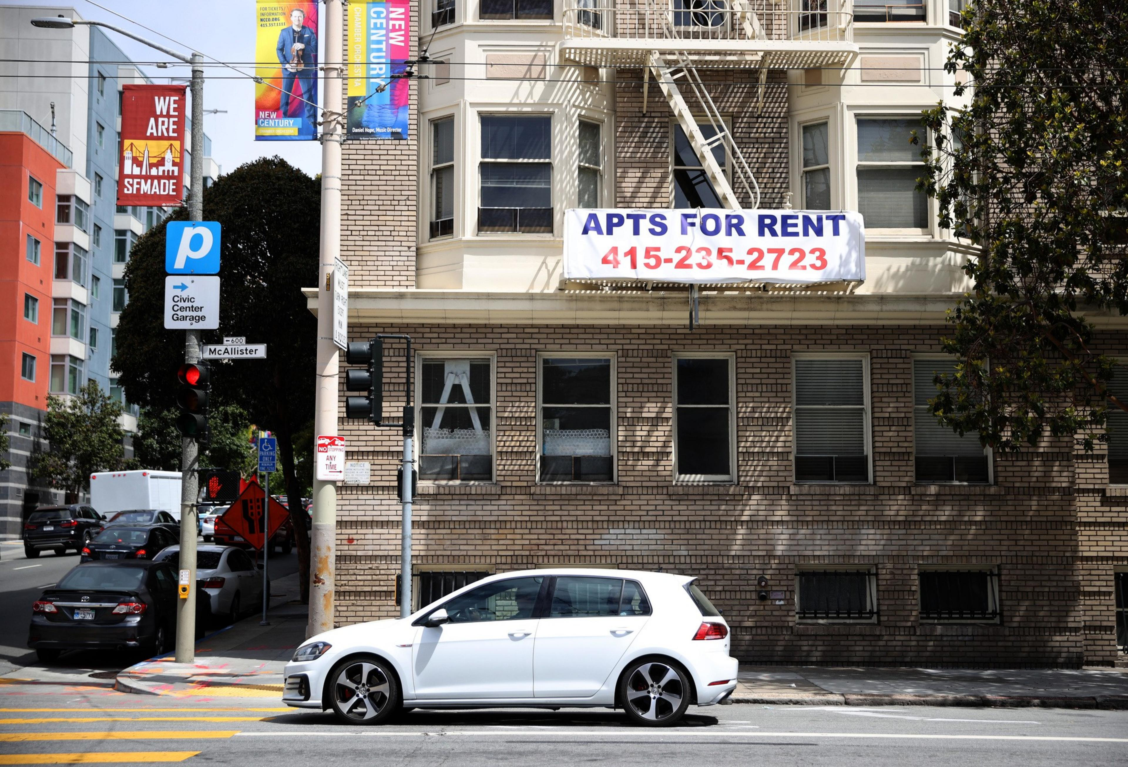 A white hatchback car is parked on the street in front of a brick ...