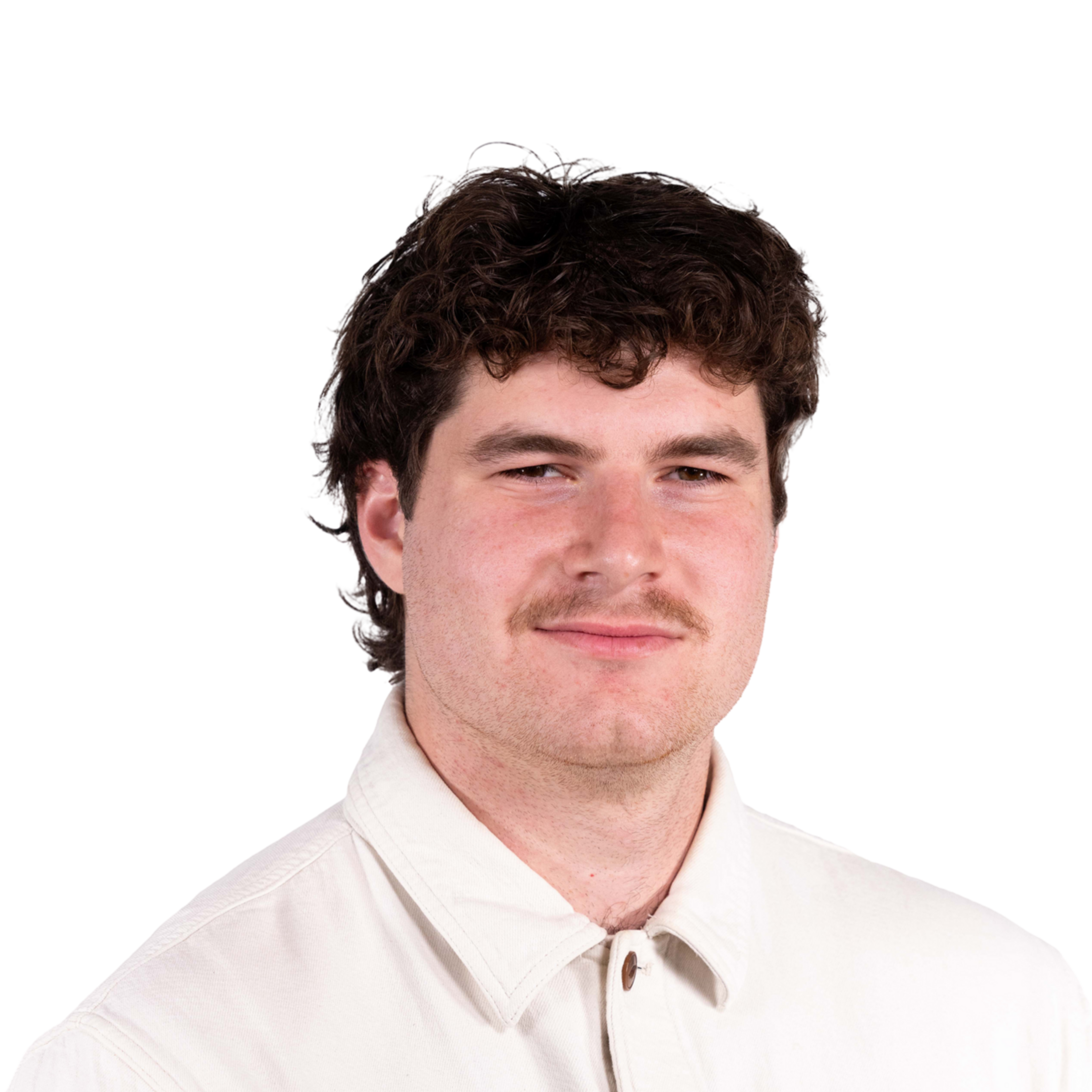 A young man with curly dark hair and a mustache wears a cream-colored ...