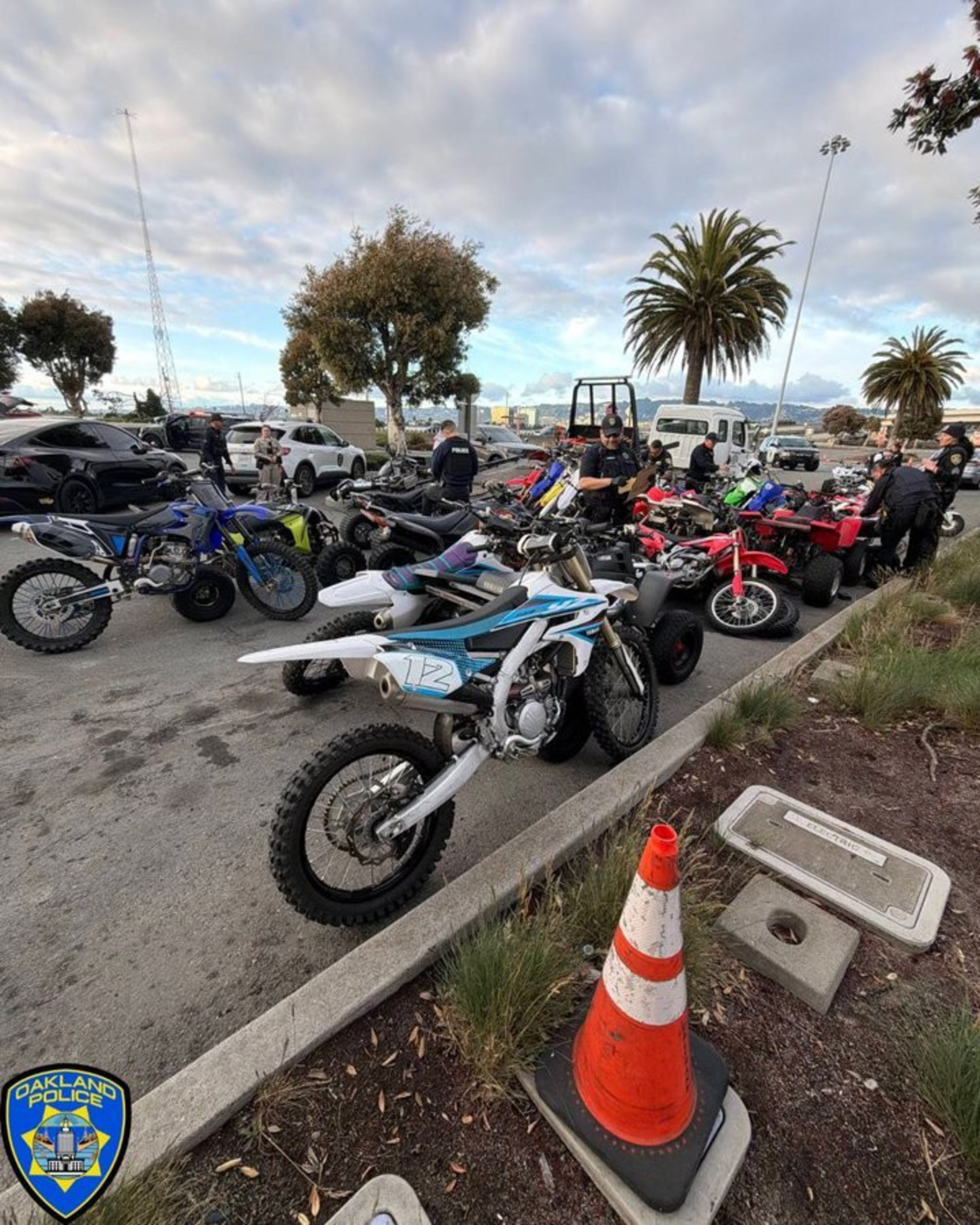 A lineup of dirt bikes and ATVs is parked on a street with several ...