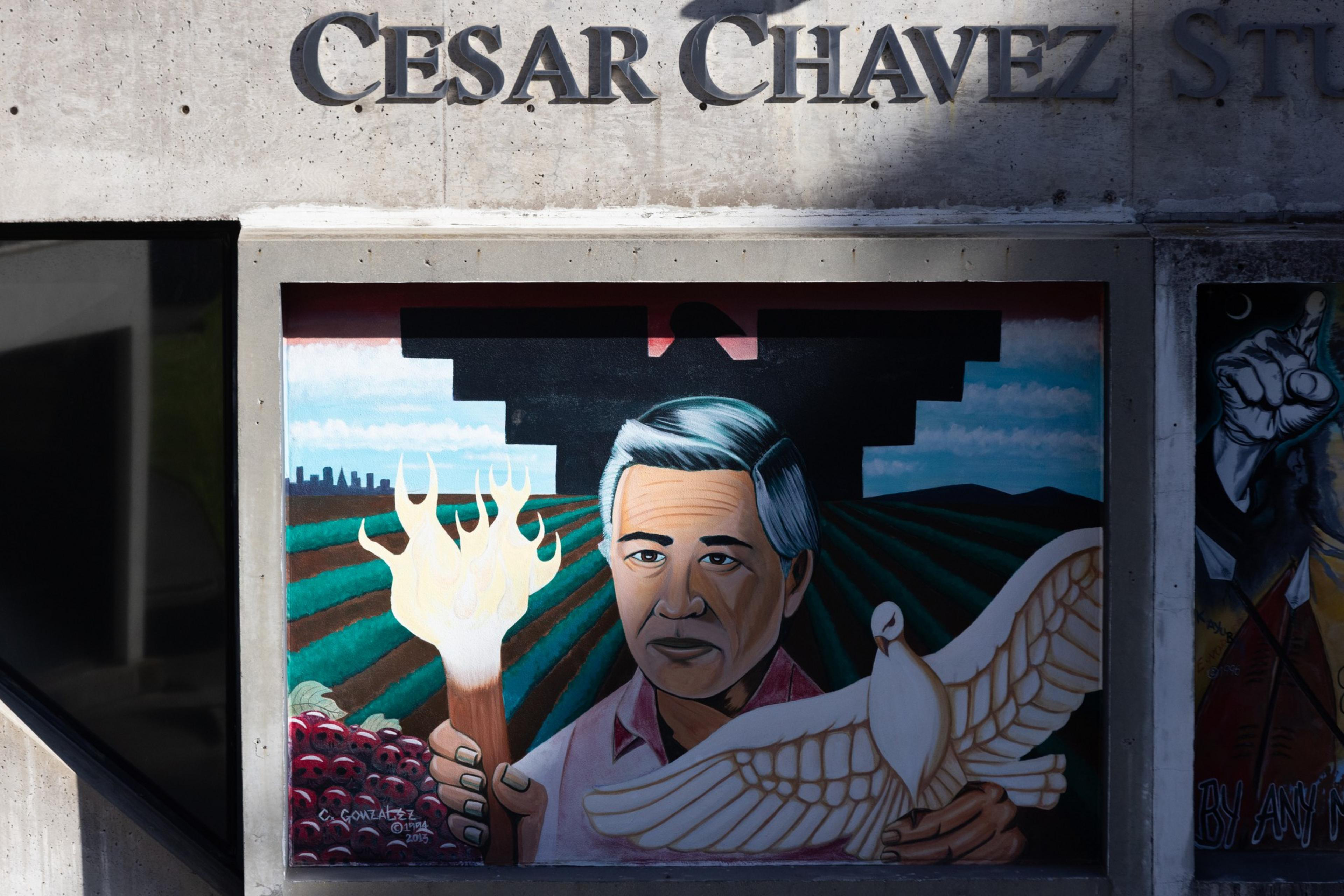 A mural of Cesar Chavez holding a flaming torch in one hand and a white ...