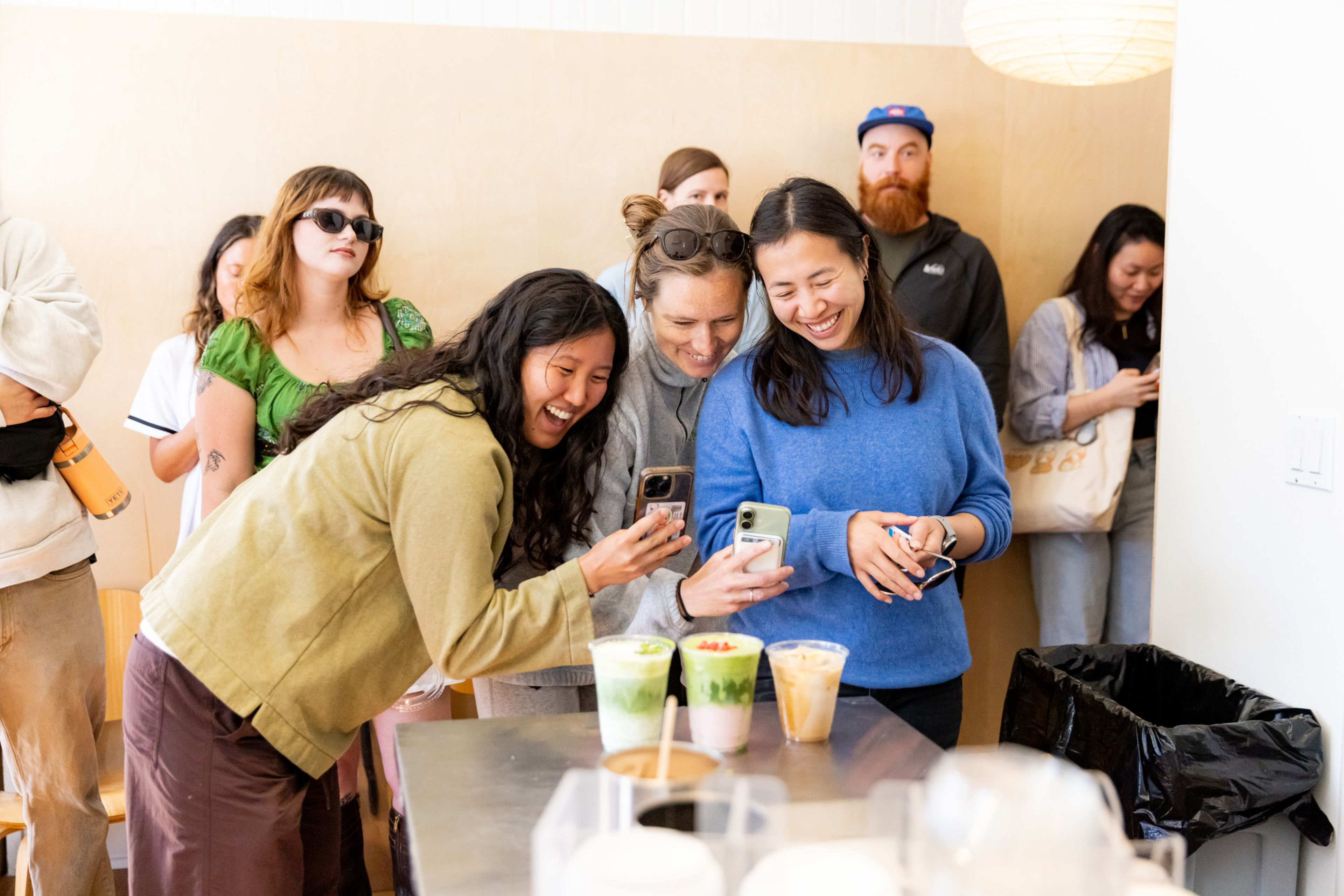 Three women laugh and take photos of drinks on a table, while several ...