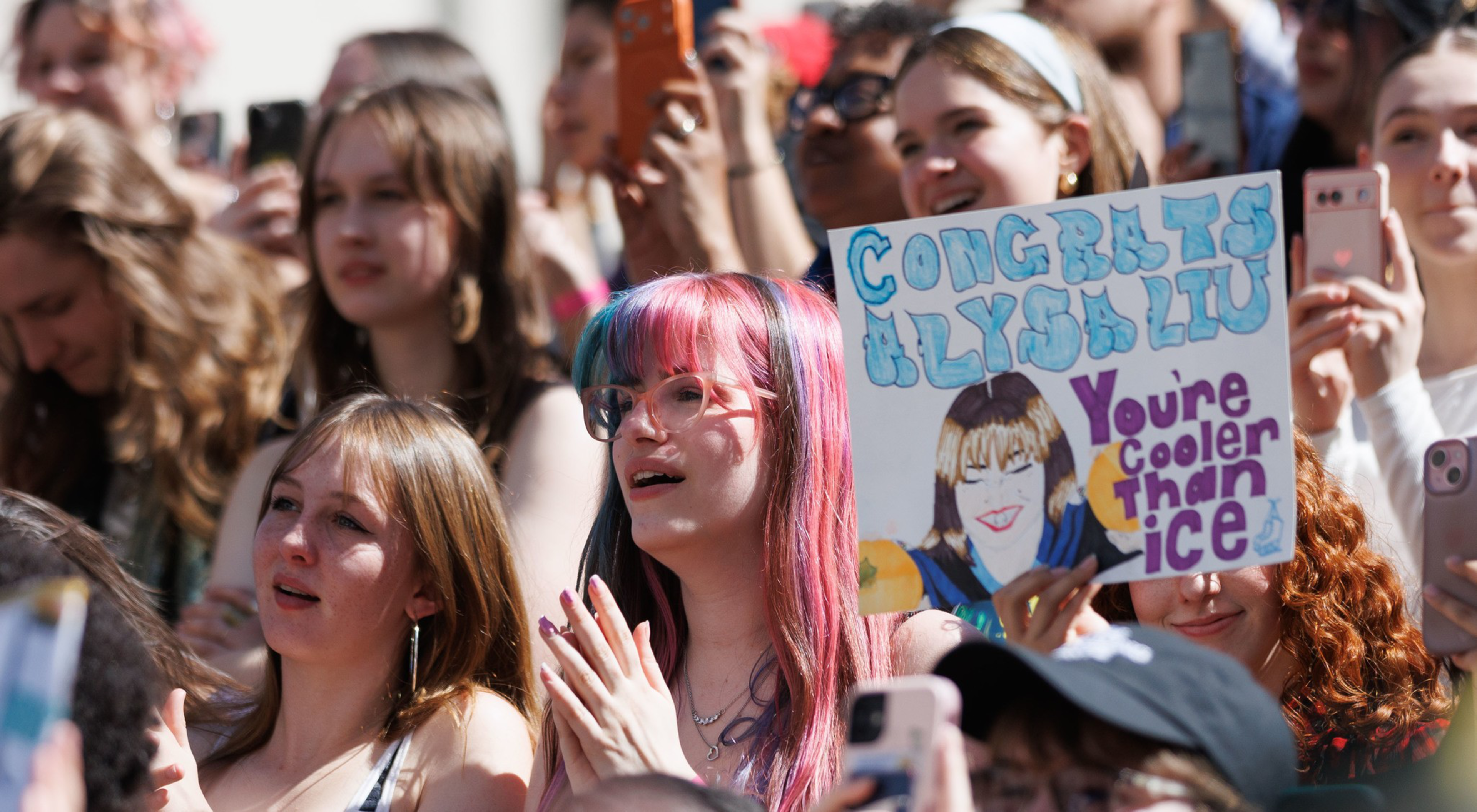 A crowd of young people, many holding phones, with one person holding a ...
